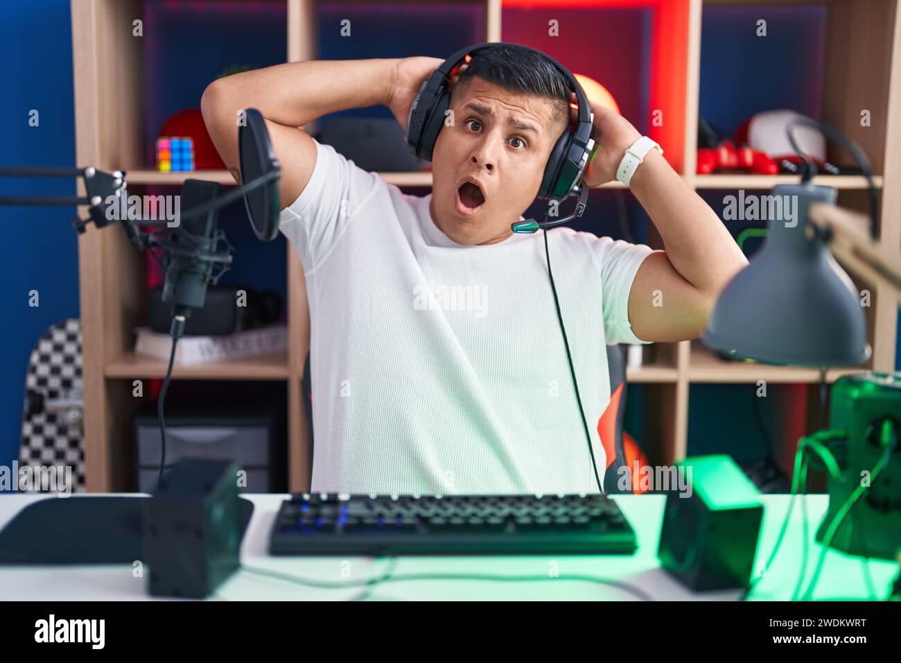 Young hispanic man playing video games crazy and scared with hands on ...