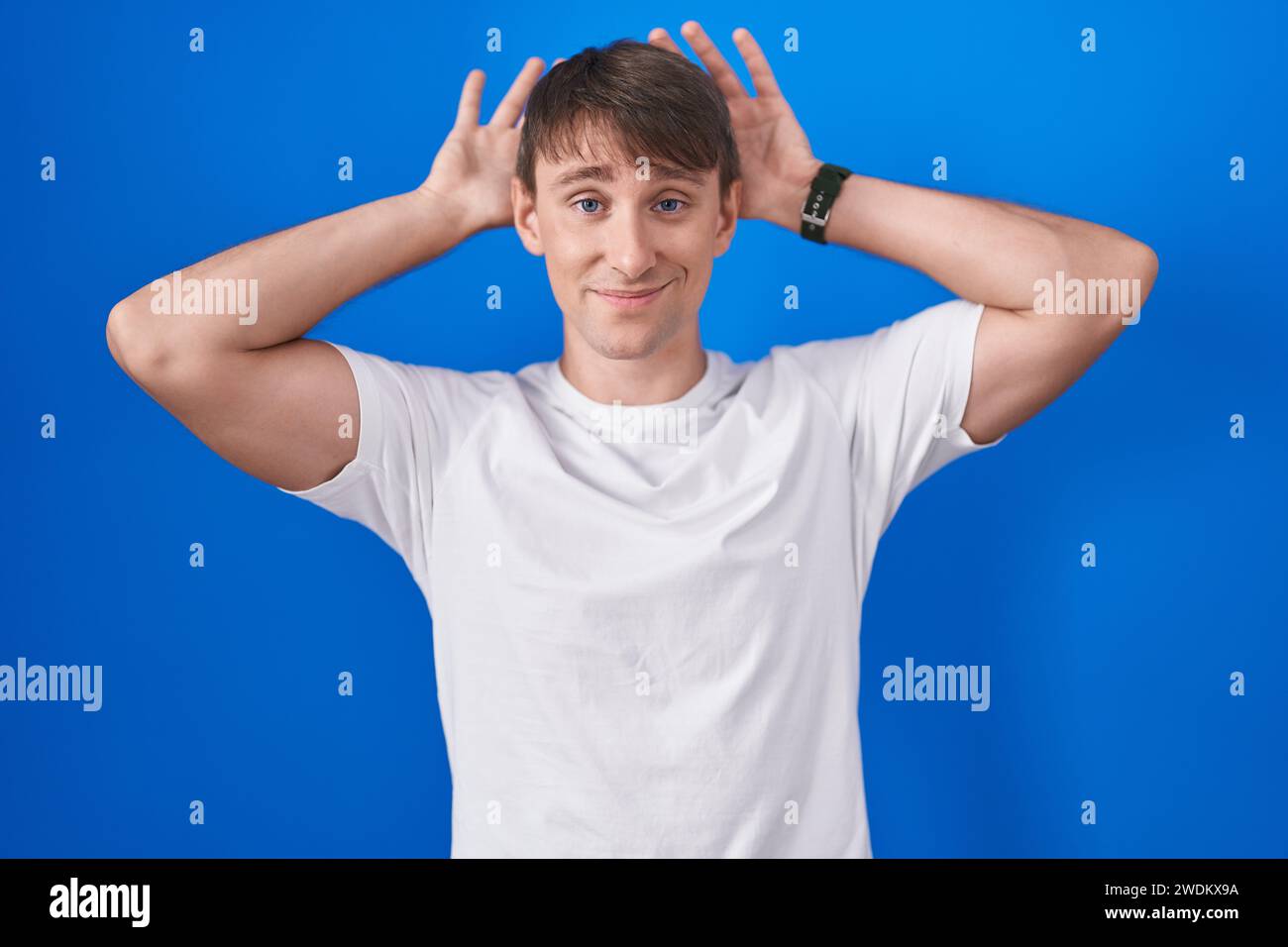 Caucasian blond man standing over blue background doing bunny ears ...