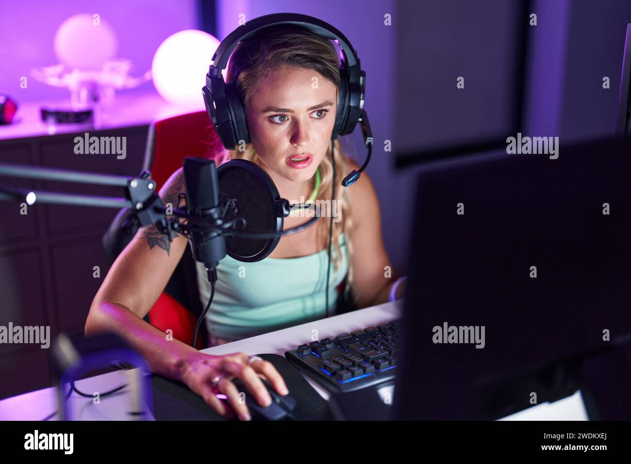 Young blonde woman streamer playing video game using computer at gaming ...