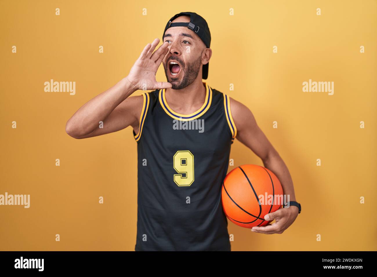 Middle age bald man holding basketball ball over yellow background ...