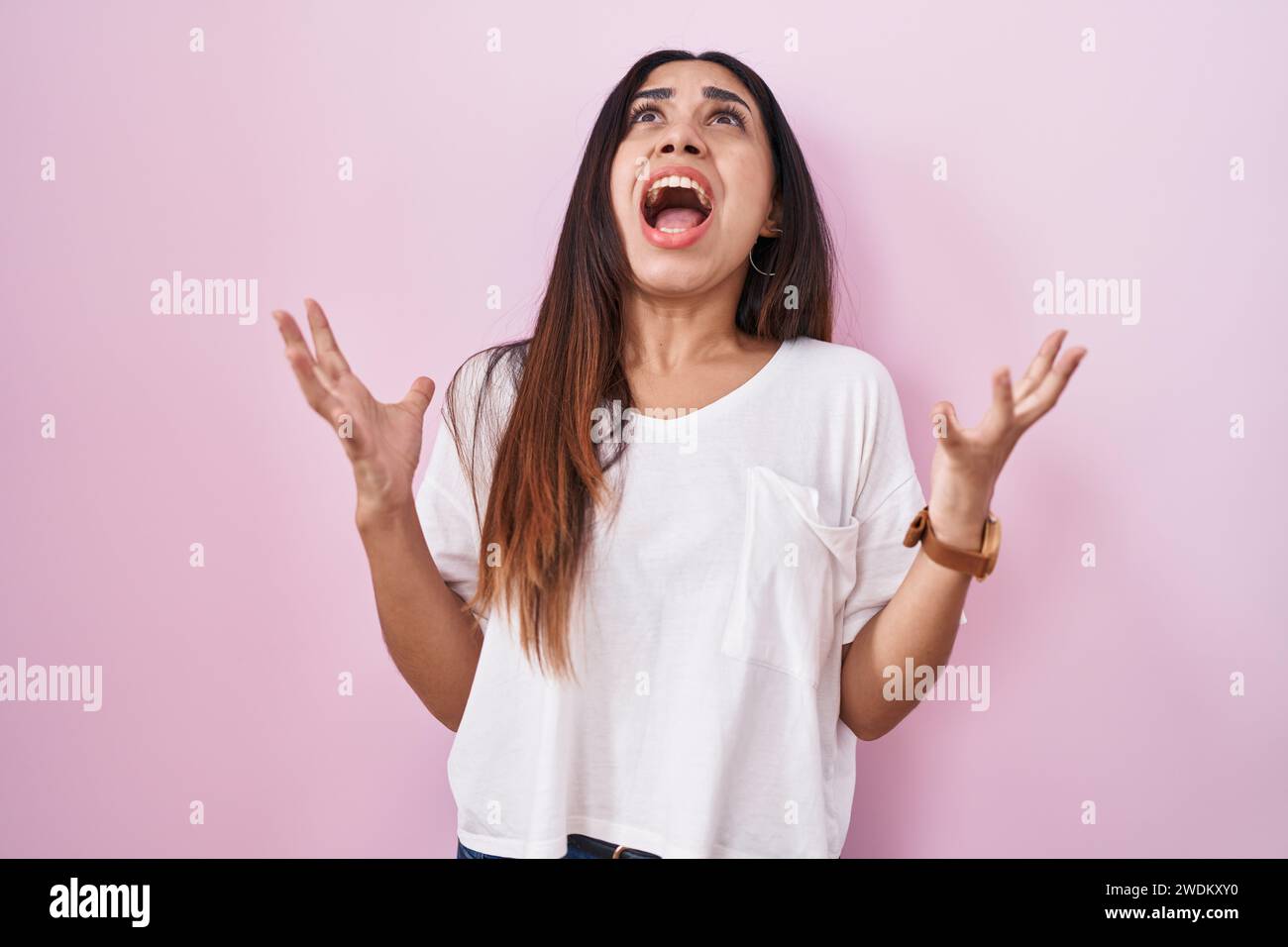 Young arab woman standing over pink background crazy and mad shouting ...