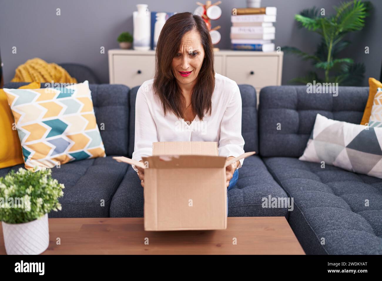 Middle age brunette woman opening cardboard box clueless and confused ...