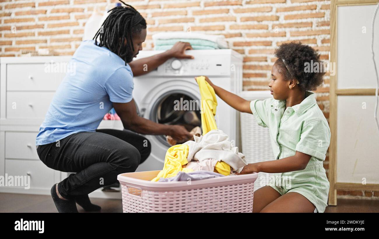 African american father and daughter washing clothes at laundry room ...