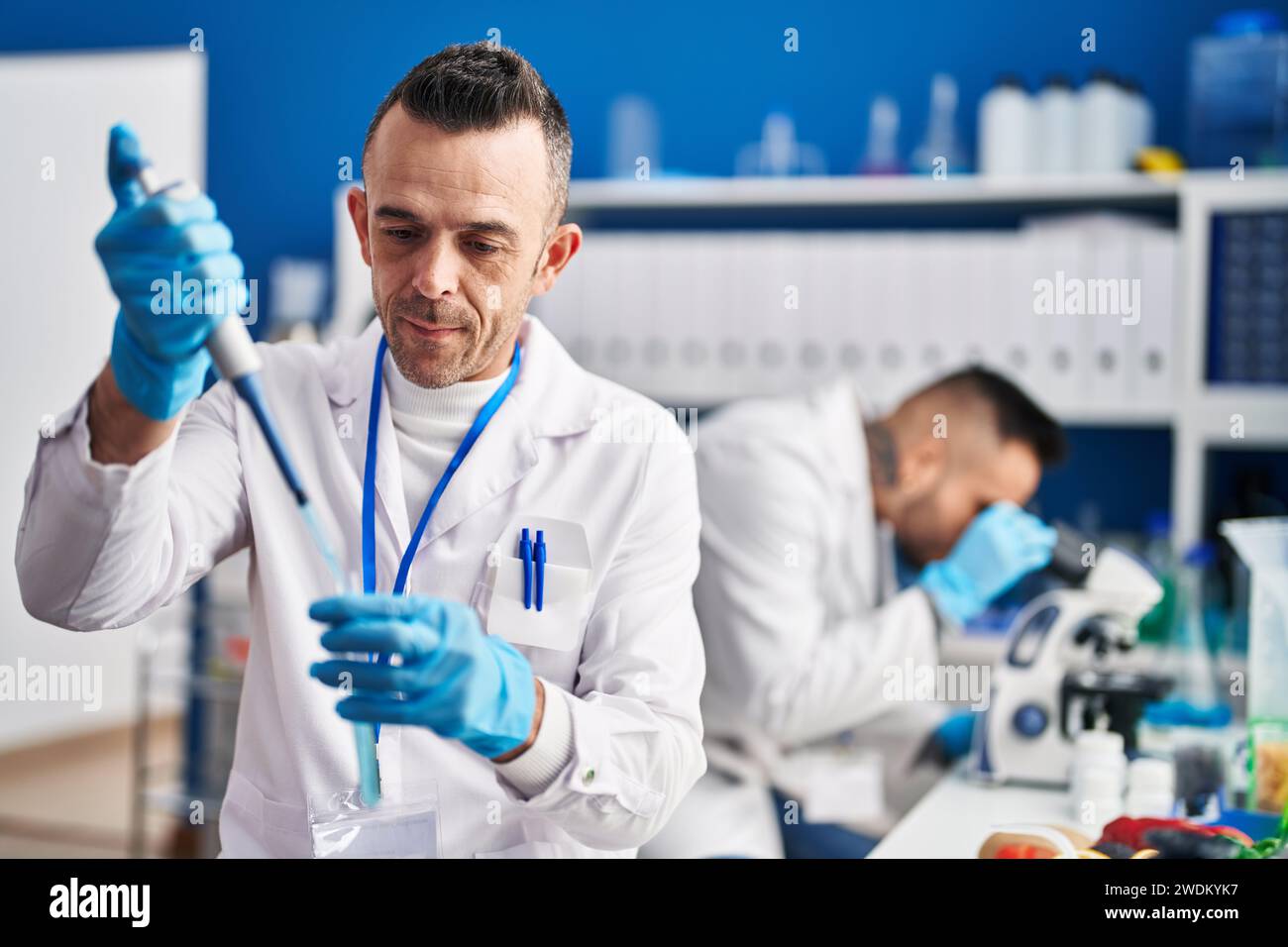 Two men scientists pouring liquid on test tube using microscope at ...