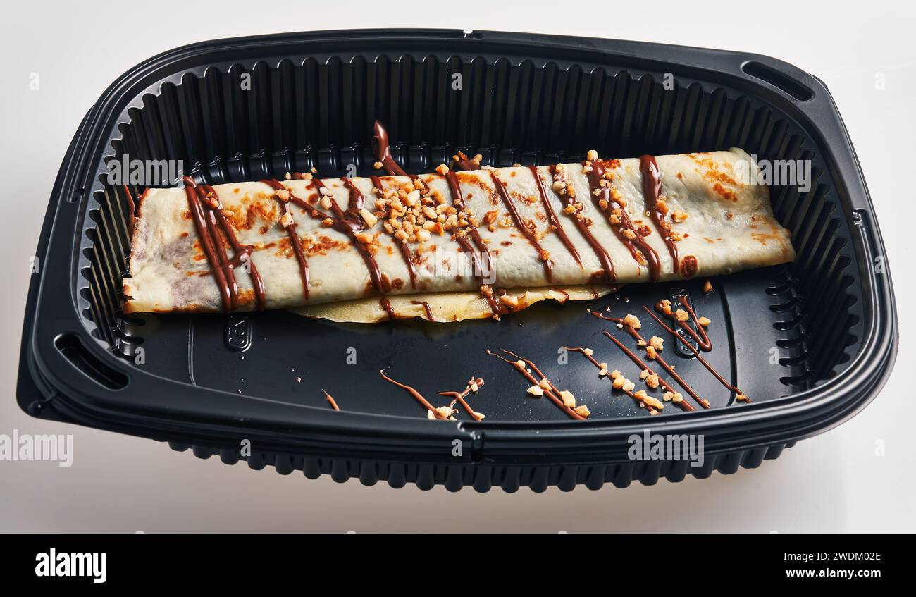 A delicious crepe with chocolate and nuts in a black takeout container ...