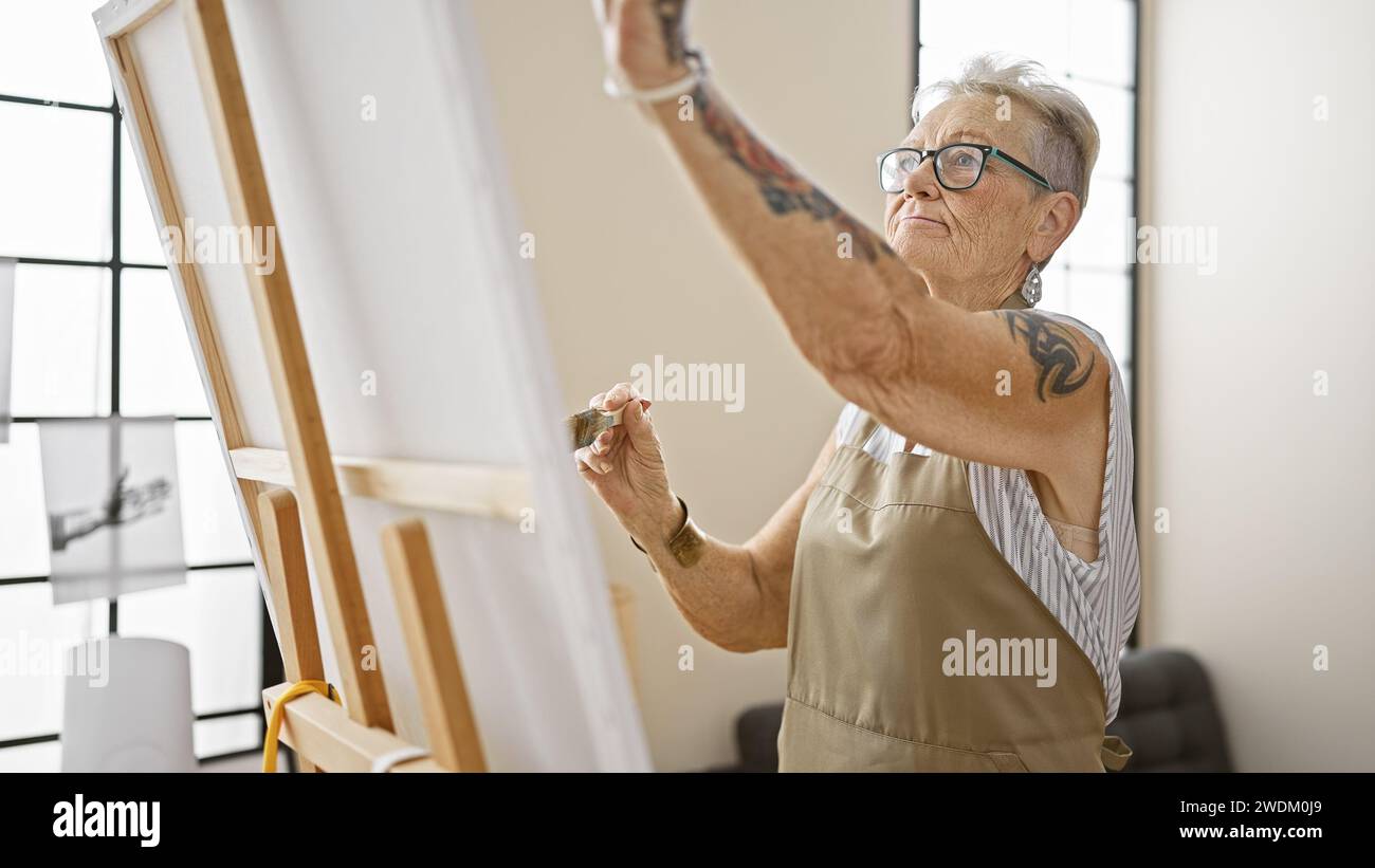 Serious, grey-haired senior woman in apron seriously concentrates on ...