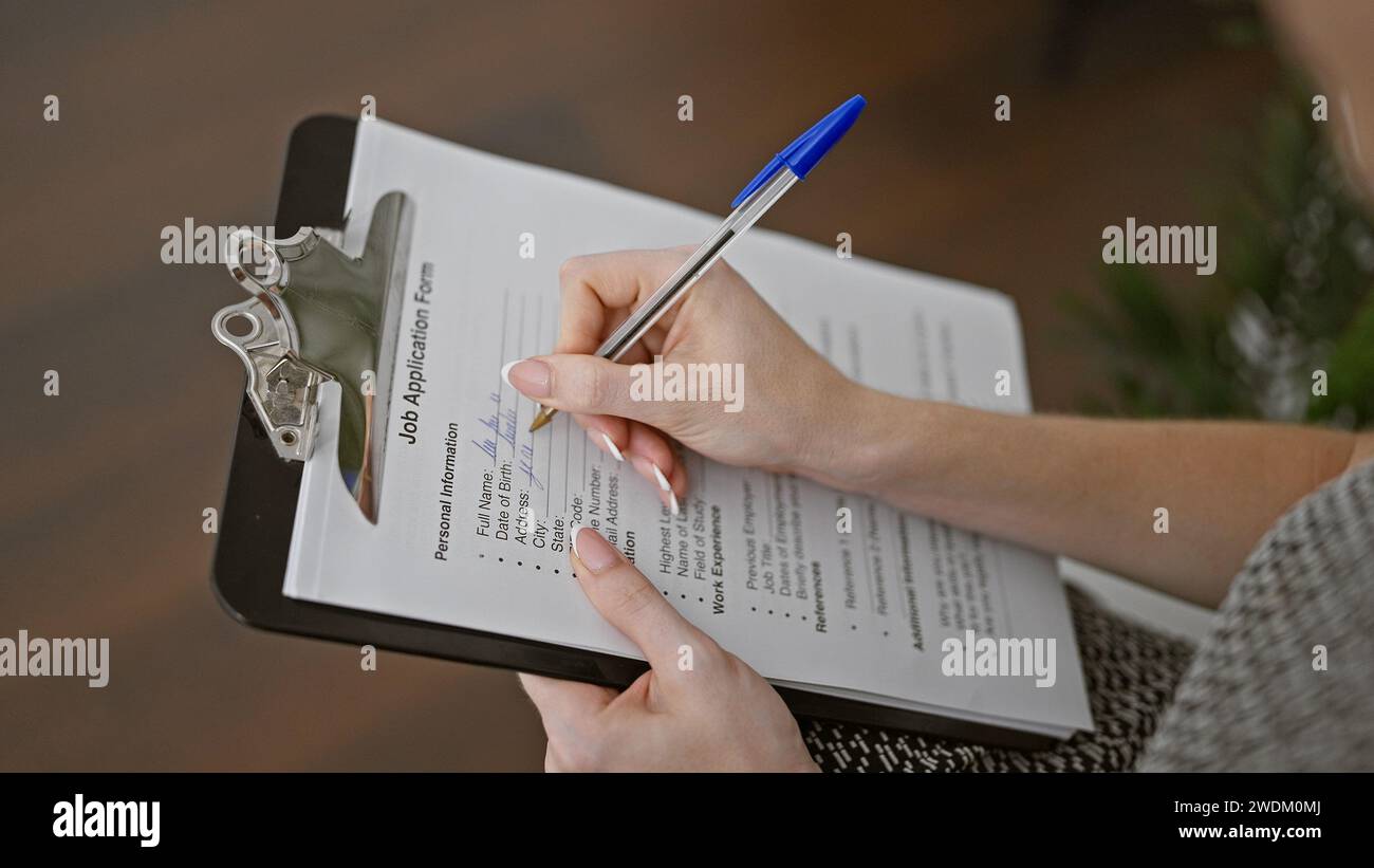 Young blonde woman sitting on chair writing on document at waiting room ...