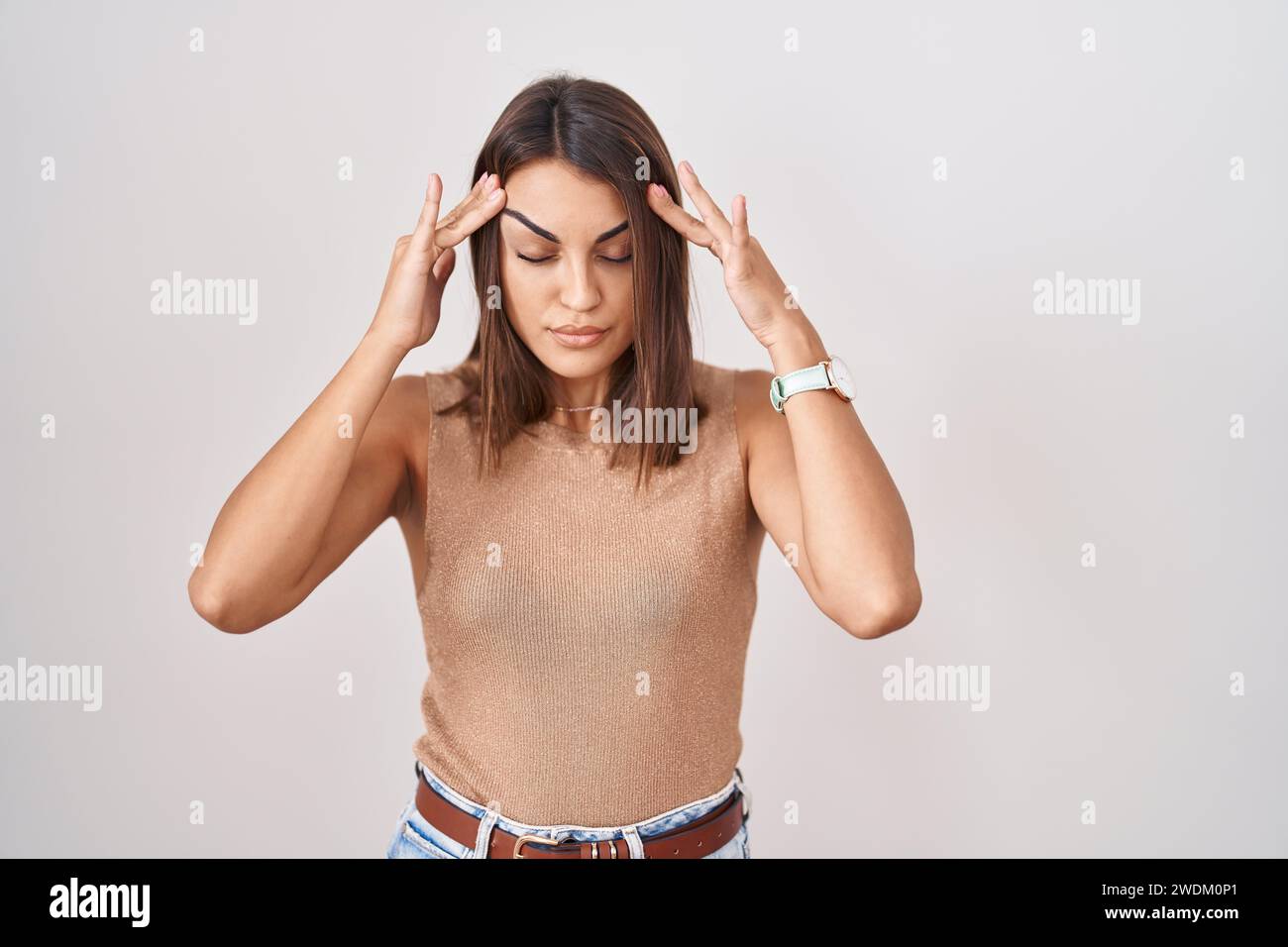 Young hispanic woman standing over white background with hand on head ...