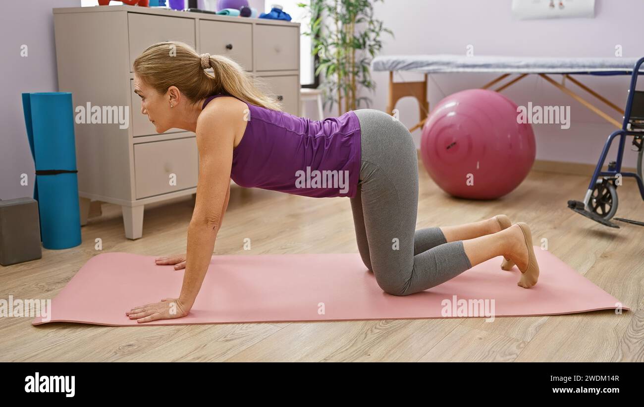 A middle-aged woman performs a tabletop exercise in a brightly-lit ...
