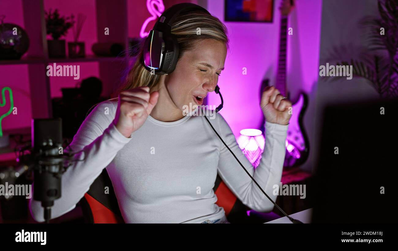 A young caucasian woman enjoys gaming at night in a dark, colorful room ...