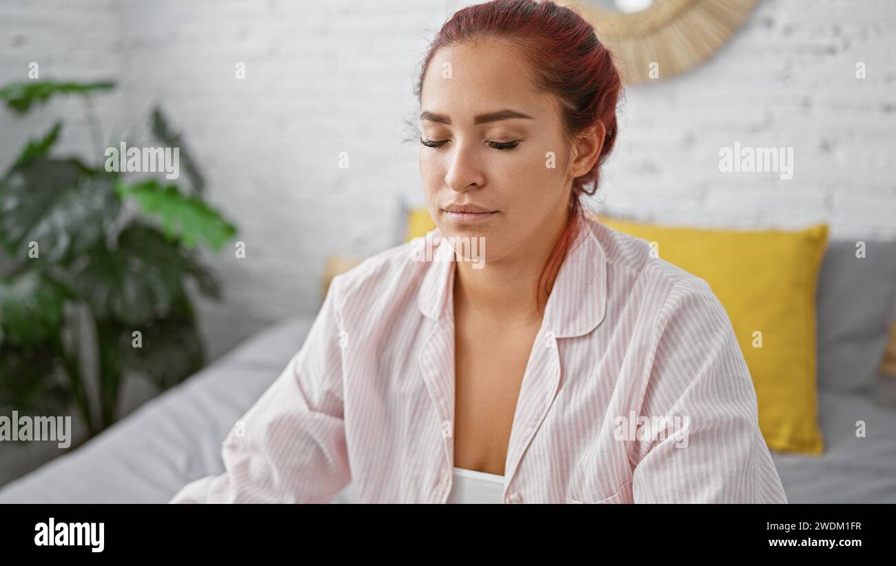 Beautiful young redhead woman sitting on bed, concentrating with closed ...