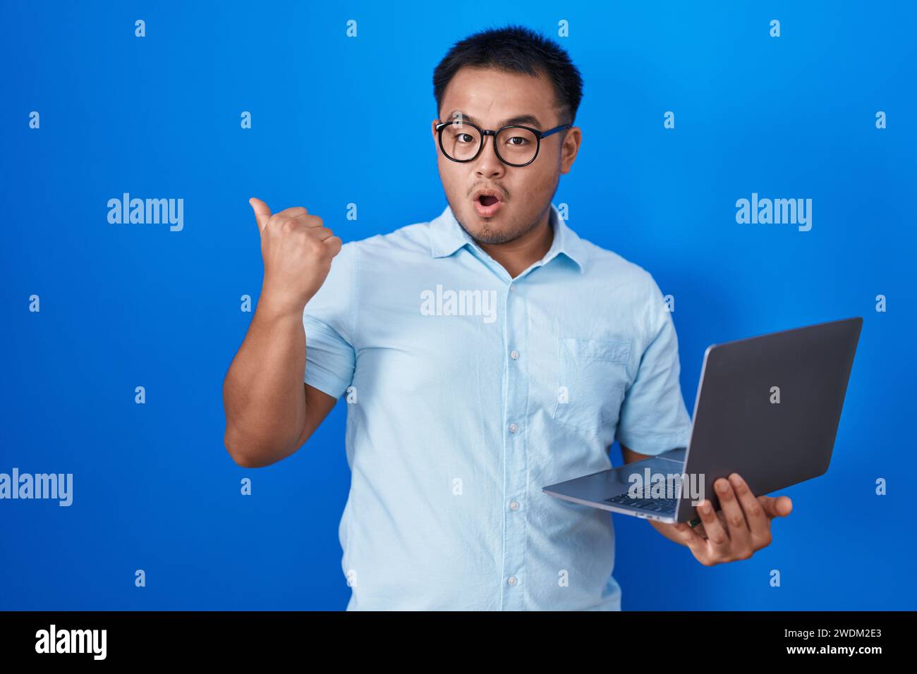 Chinese young man using computer laptop surprised pointing with hand ...