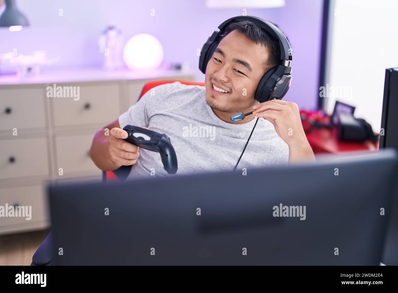 Young chinese man streamer playing video game using joystick at gaming ...