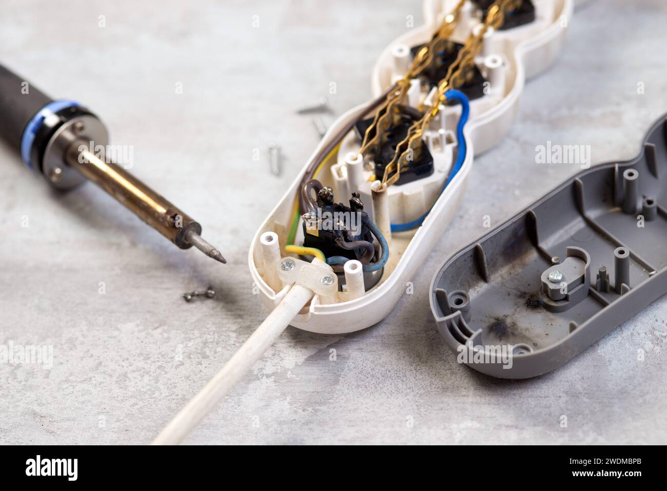 Old burnt extension cord with soldering iron on gray background close ...