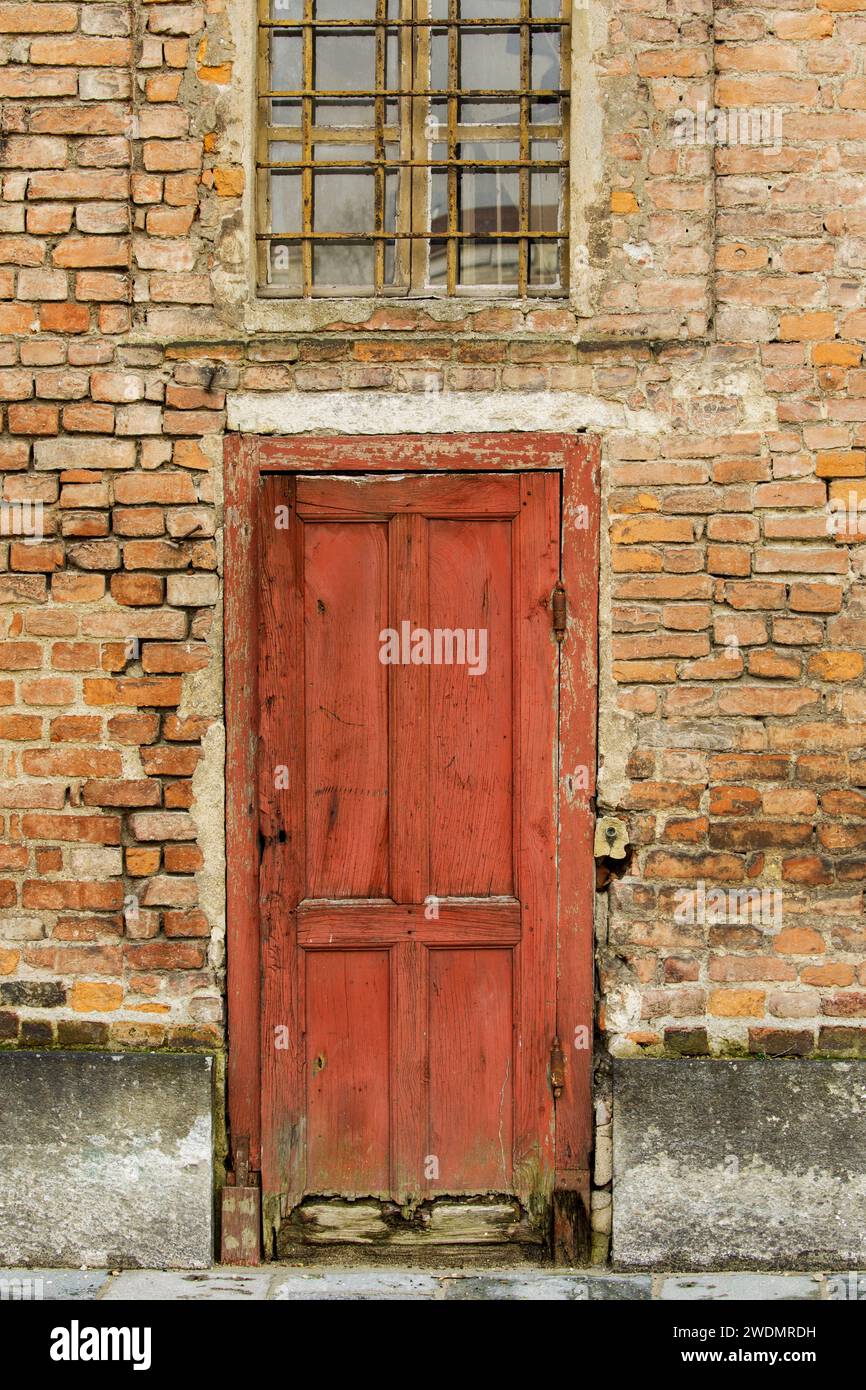 Old red door in a medieval red brick wall with window with cross bars ...