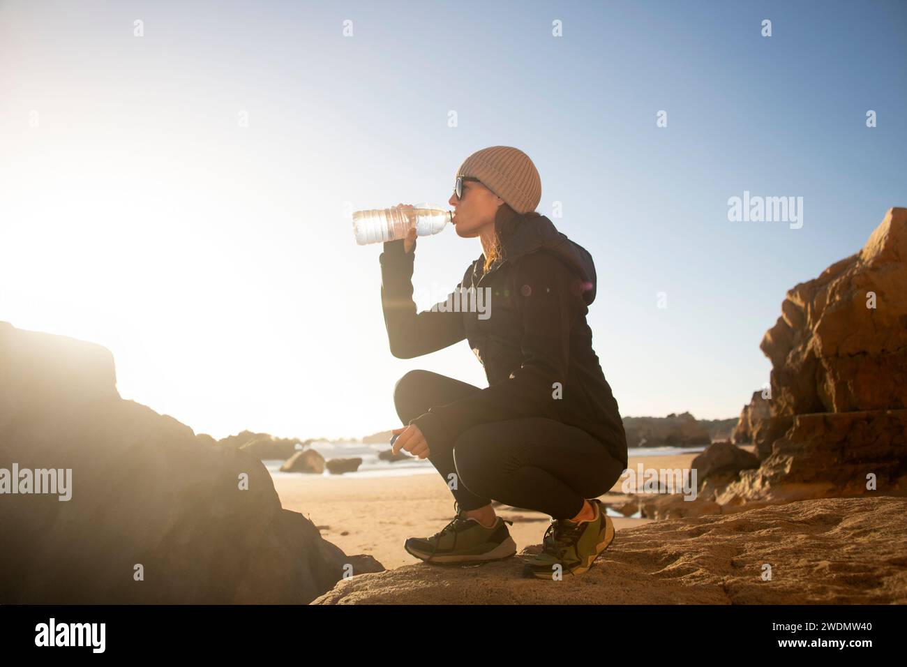 Female walker resting and drinking water on top of rocks with blue sky ...