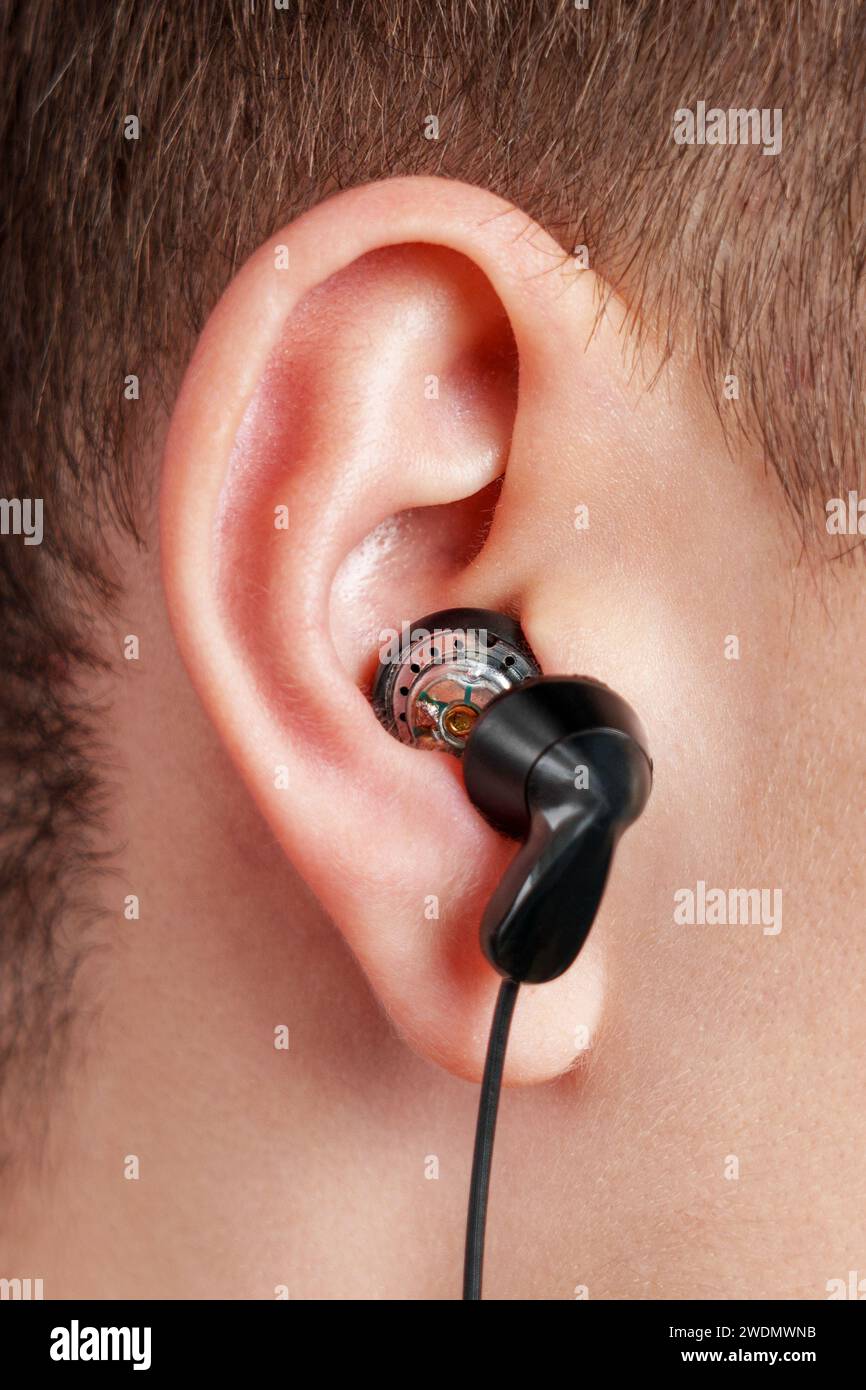 A broken headphone in the ear of a young man in close-up. Vertical view ...