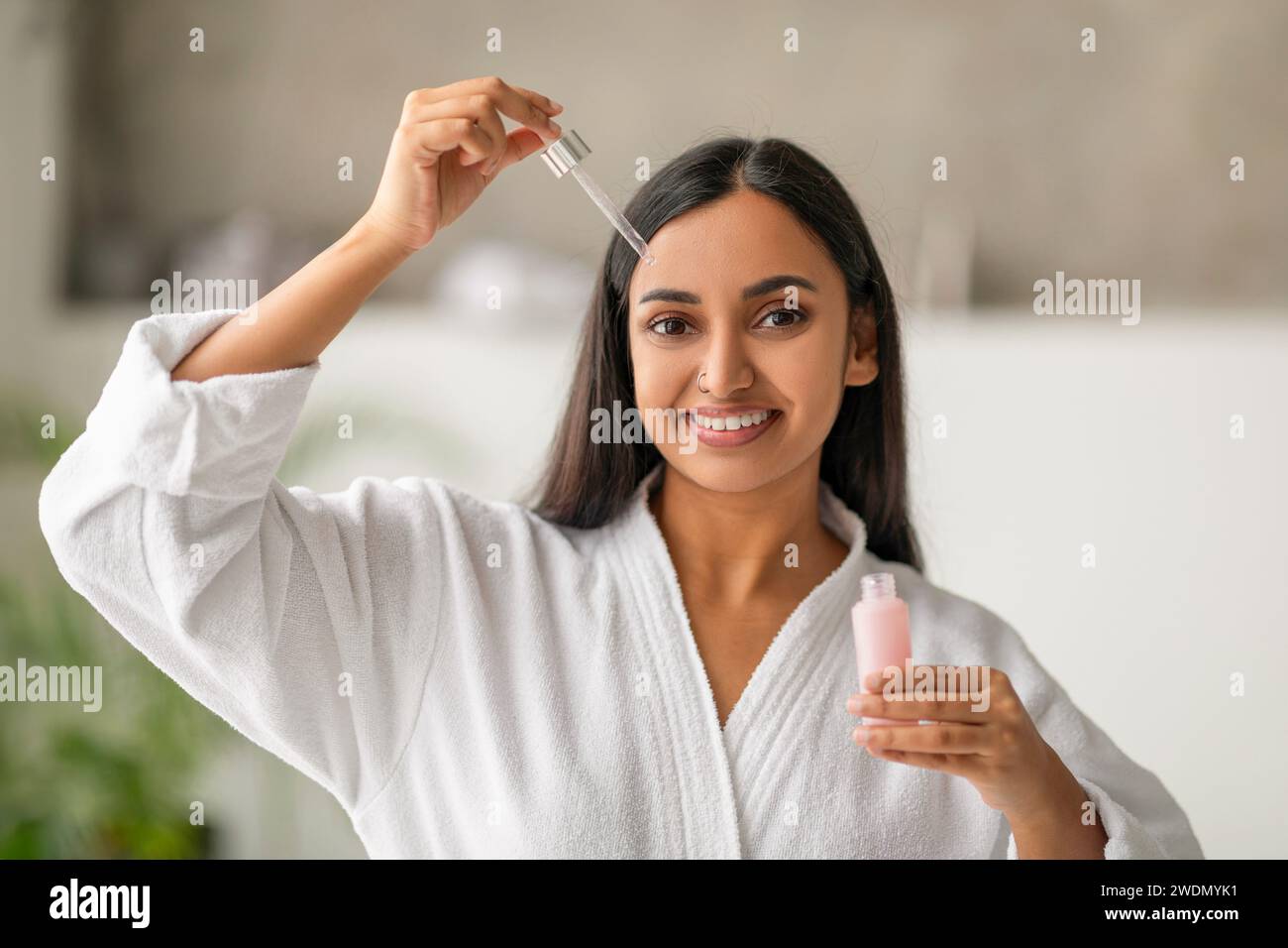 Attractive young indian woman applying moisturizing serum onto her face ...