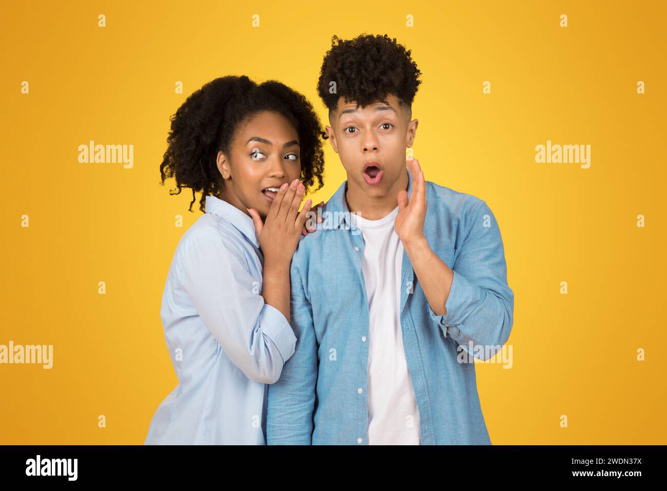 A young woman whispers into her hand with a mischievous expression ...