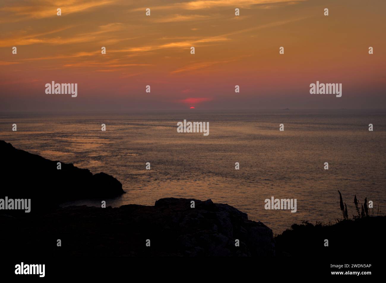The setting sun dips below the horizon at sunset on the Welsh coast on ...