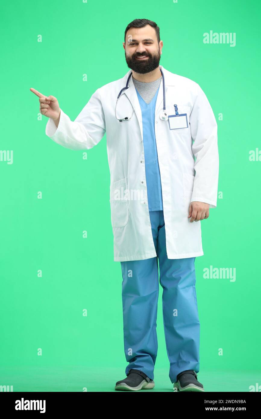 The male doctor, full-length, on a green background, points to the side ...