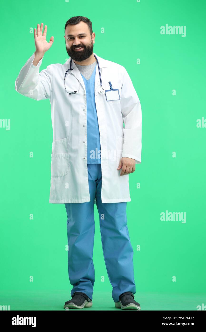 A male doctor, full-length, on a green background, waving his hand ...