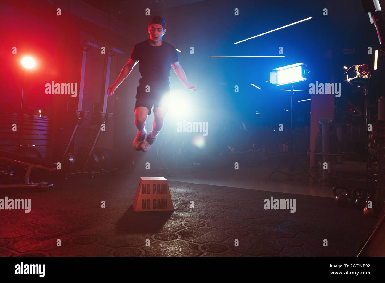 An athlete executes a box jump, soaring above 'No Pain No Gain,' amidst ...