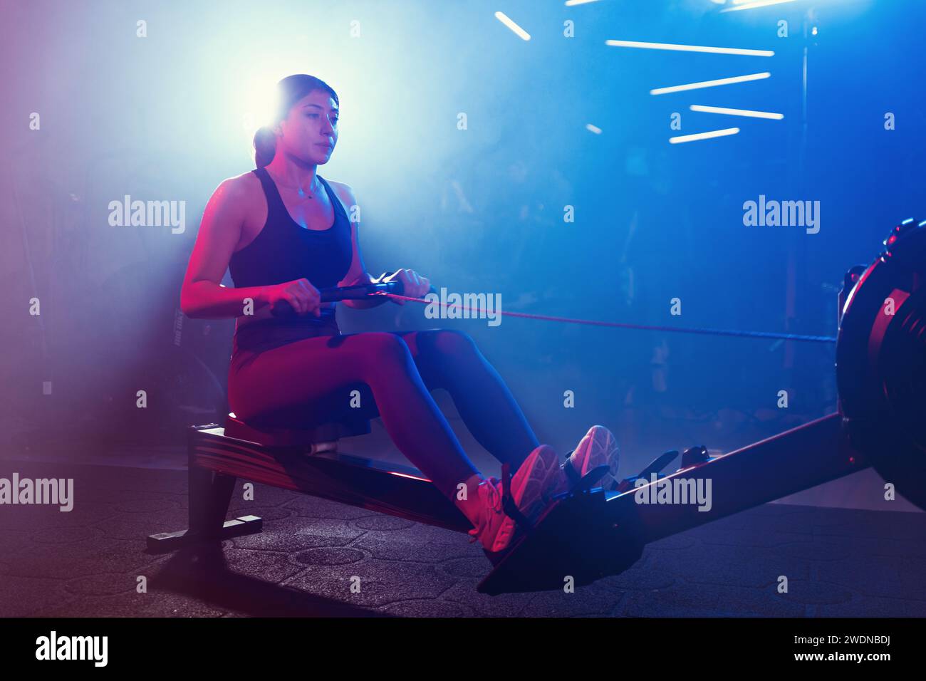 In the gym, a woman trains on a rowing machine, surrounded by a ...