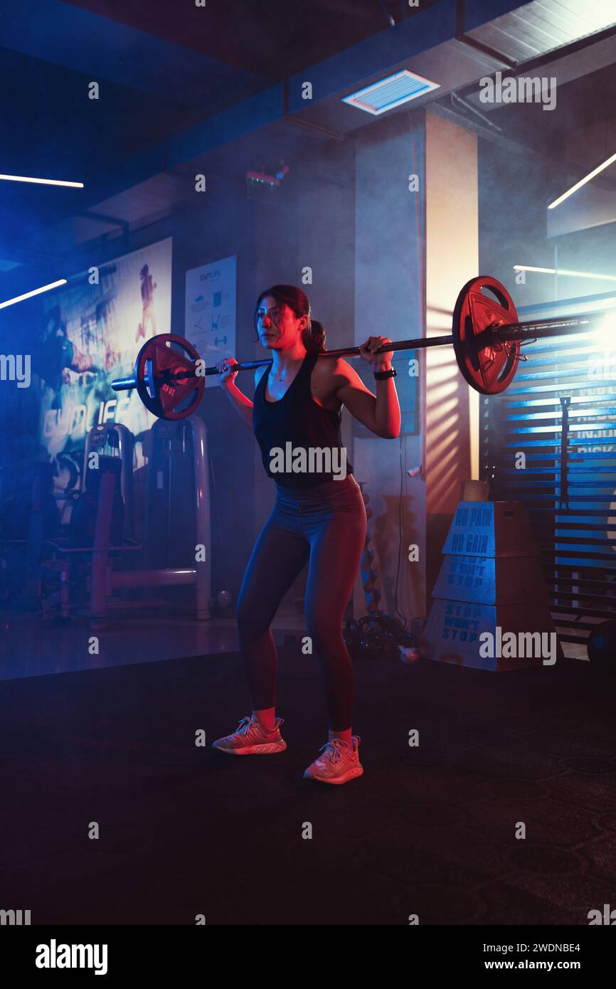 Under the watchful eye of her trainer, a female athlete squats with a ...