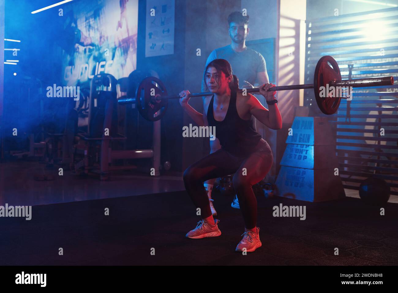 Under the watchful eye of her trainer, a female athlete squats with a ...