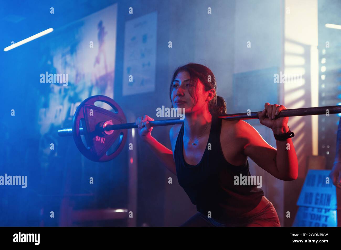 Under the watchful eye of her trainer, a female athlete squats with a ...