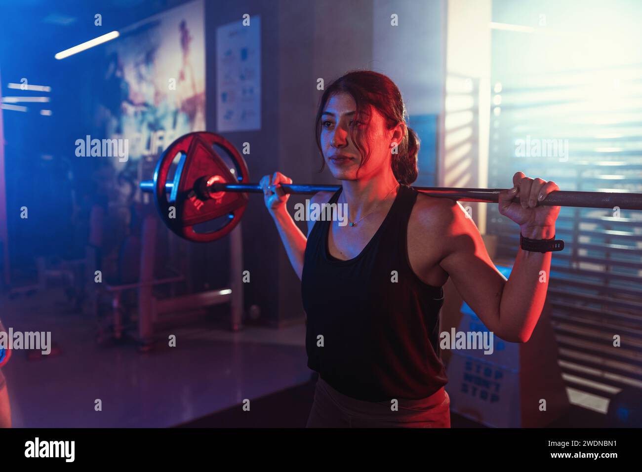 Under the watchful eye of her trainer, a female athlete squats with a ...