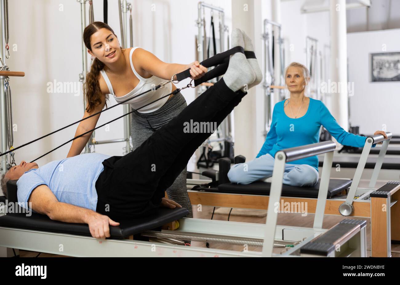 Smiling personal female trainer assisting mature man exercising on ...