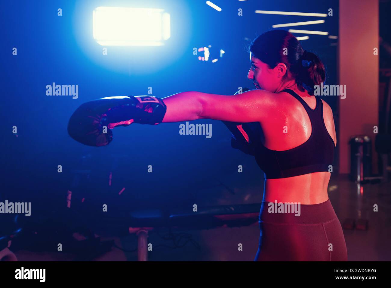 A committed female athlete practices her punches under dramatic blue ...