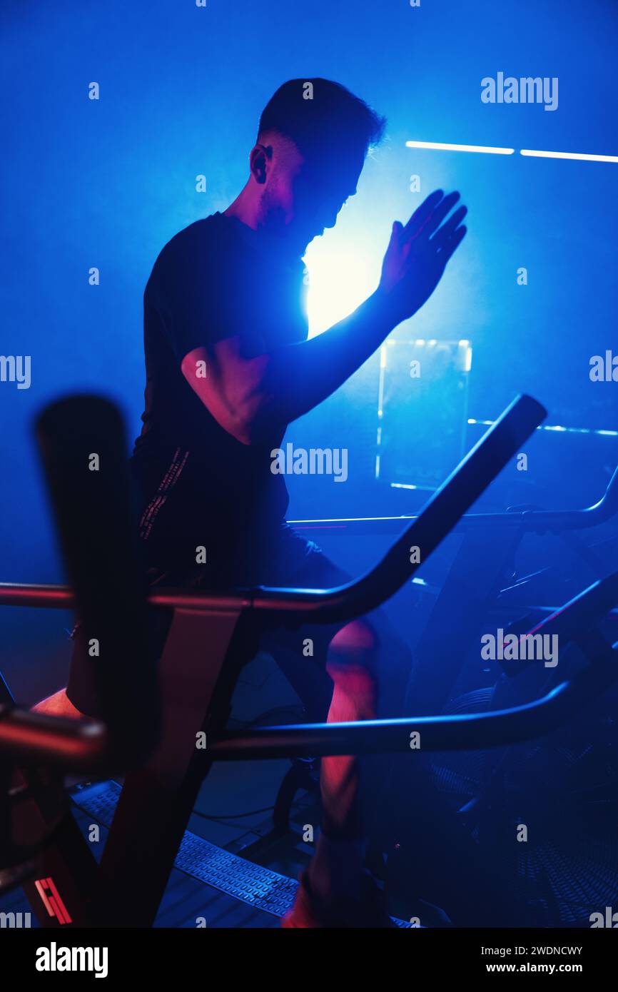 Male athlete running on a treadmill, illuminated by vivid blue and red ...