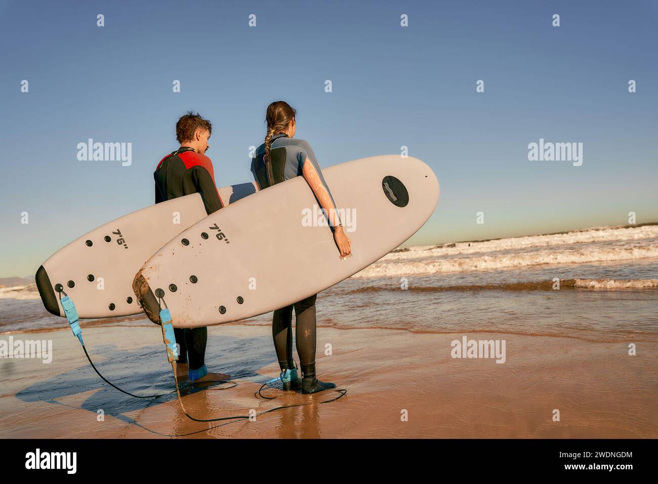 Back view of surfers in wetsuits standing with surfboards and looking ...