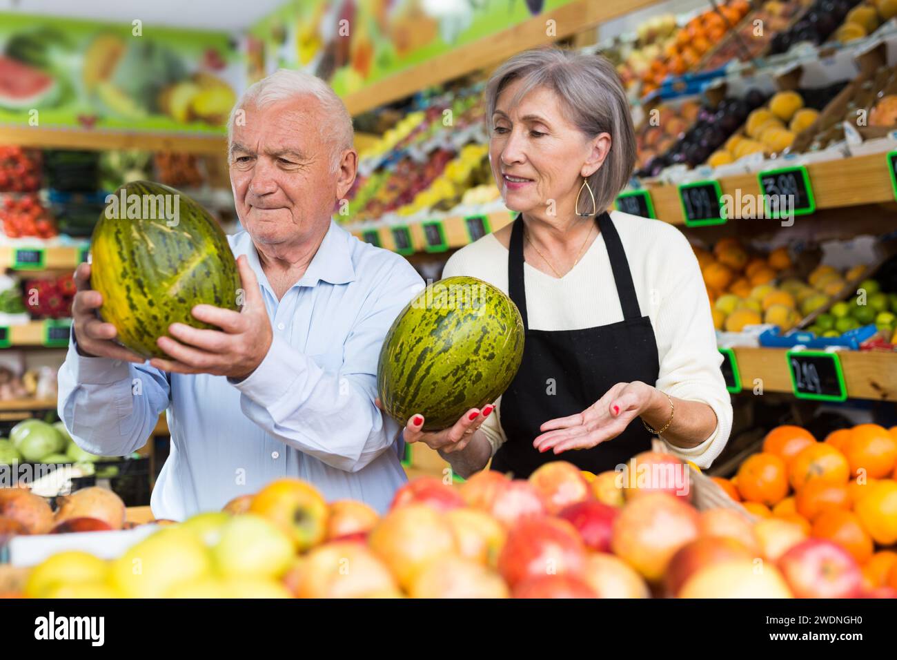 Woman supermarket employee helping mature man to choose watermelon and ...
