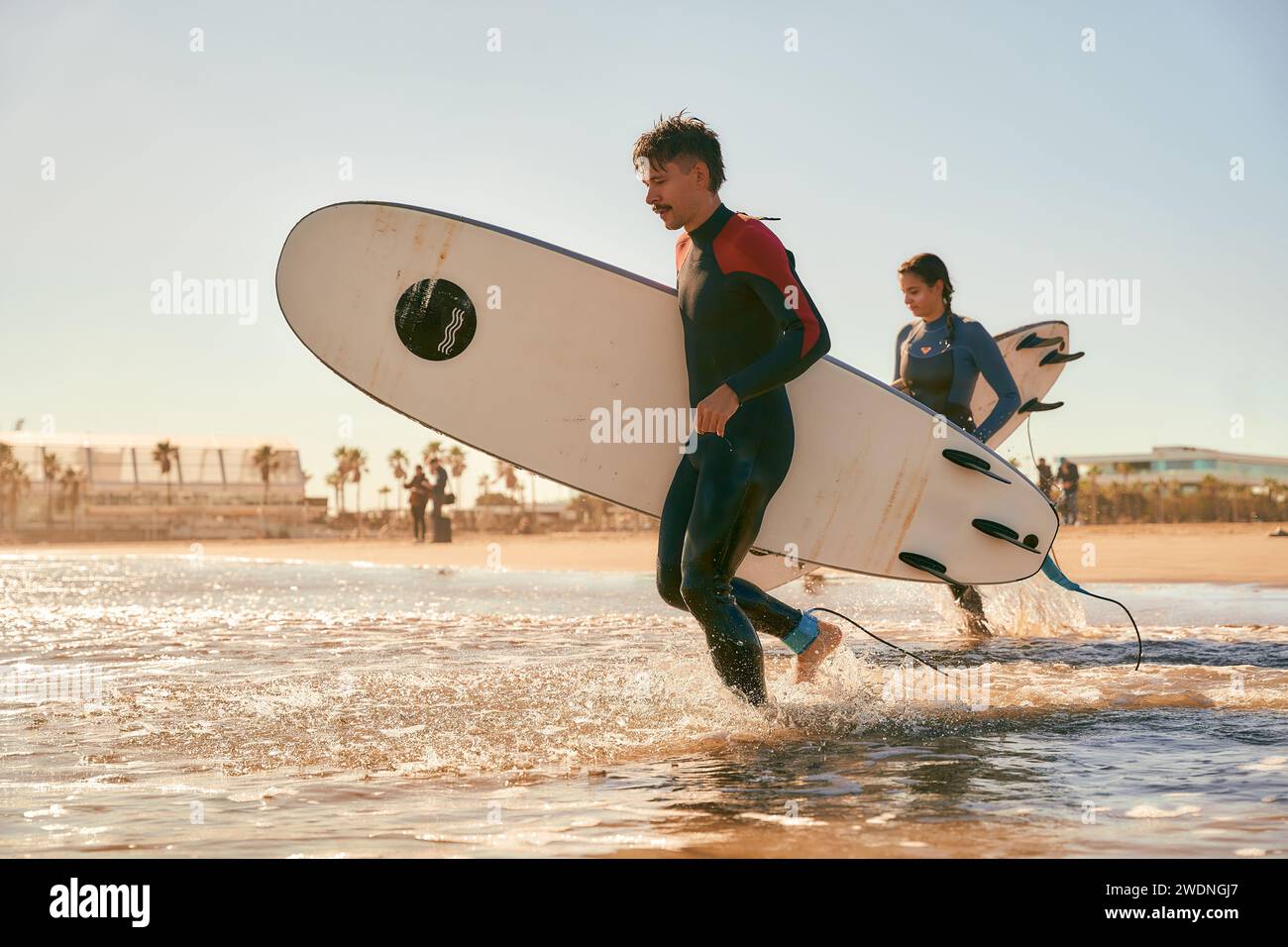 Side view of surfers in wetsuits running into the sea holding ...