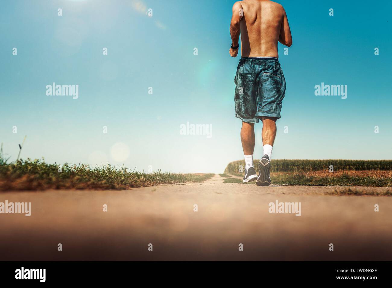 sporty man running on the road up a mountain in bright sun and blue sky ...