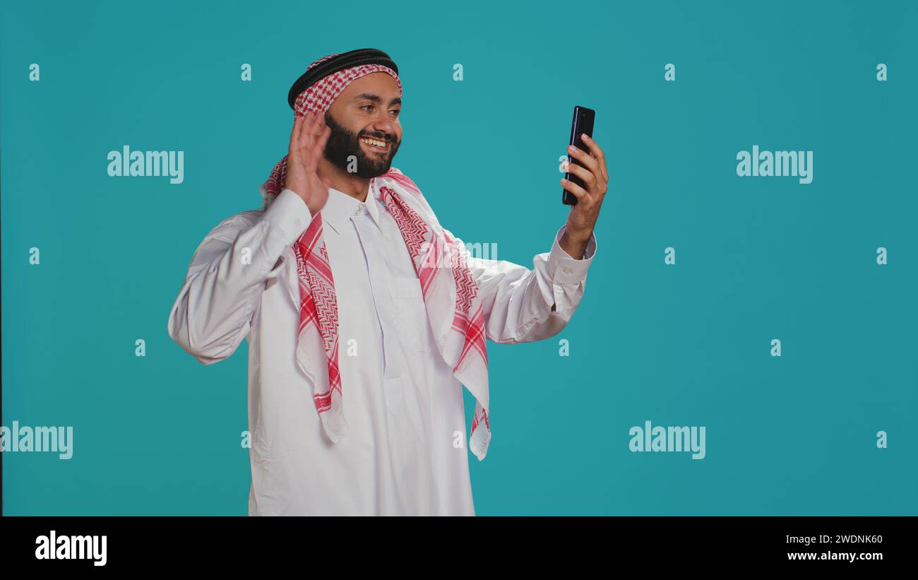 Muslim adult engages in online chat on phone, wearing traditional ...