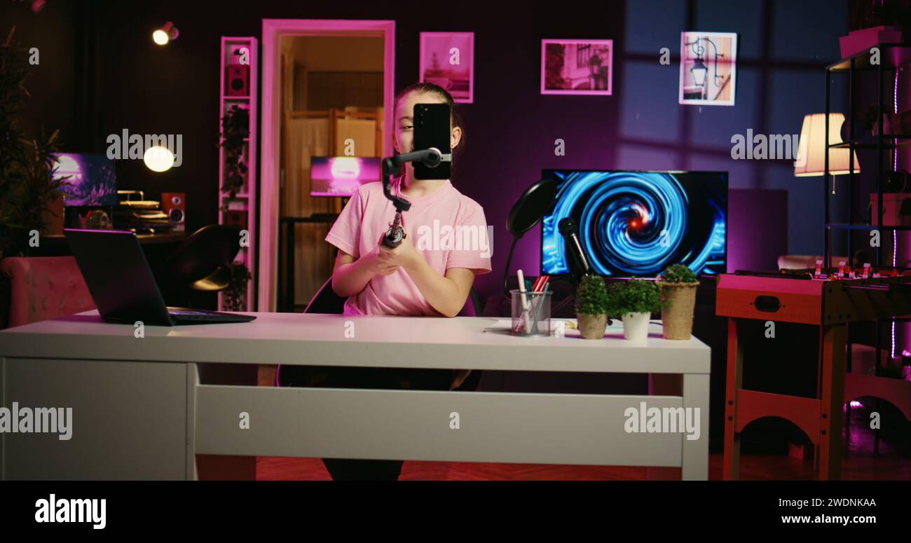 Panning shot of youngster filming video with phone on tripod in pink ...