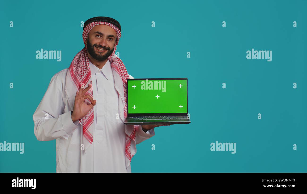 Muslim adult shows greenscreen laptop with blank mockup layout on ...