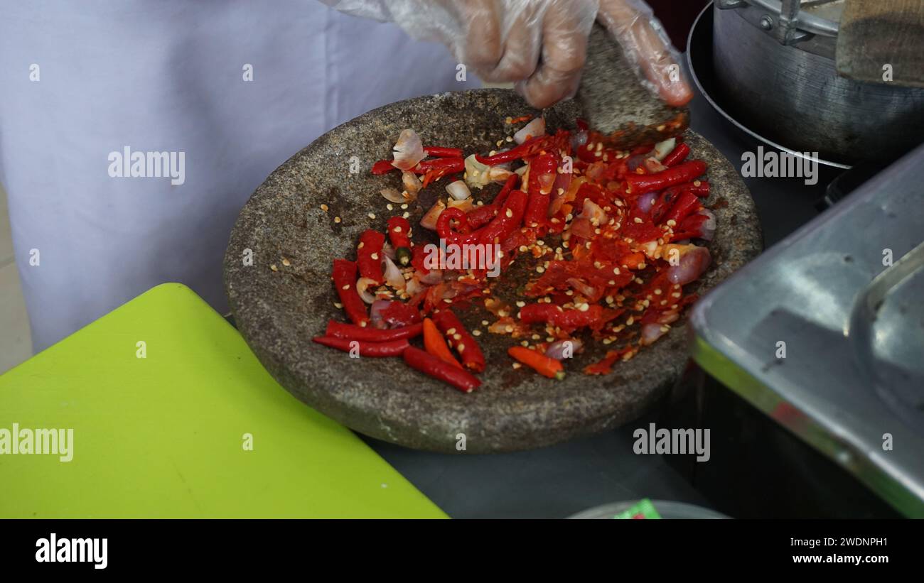 The chef is pounding chili sauce. Sambal is a famous food from ...