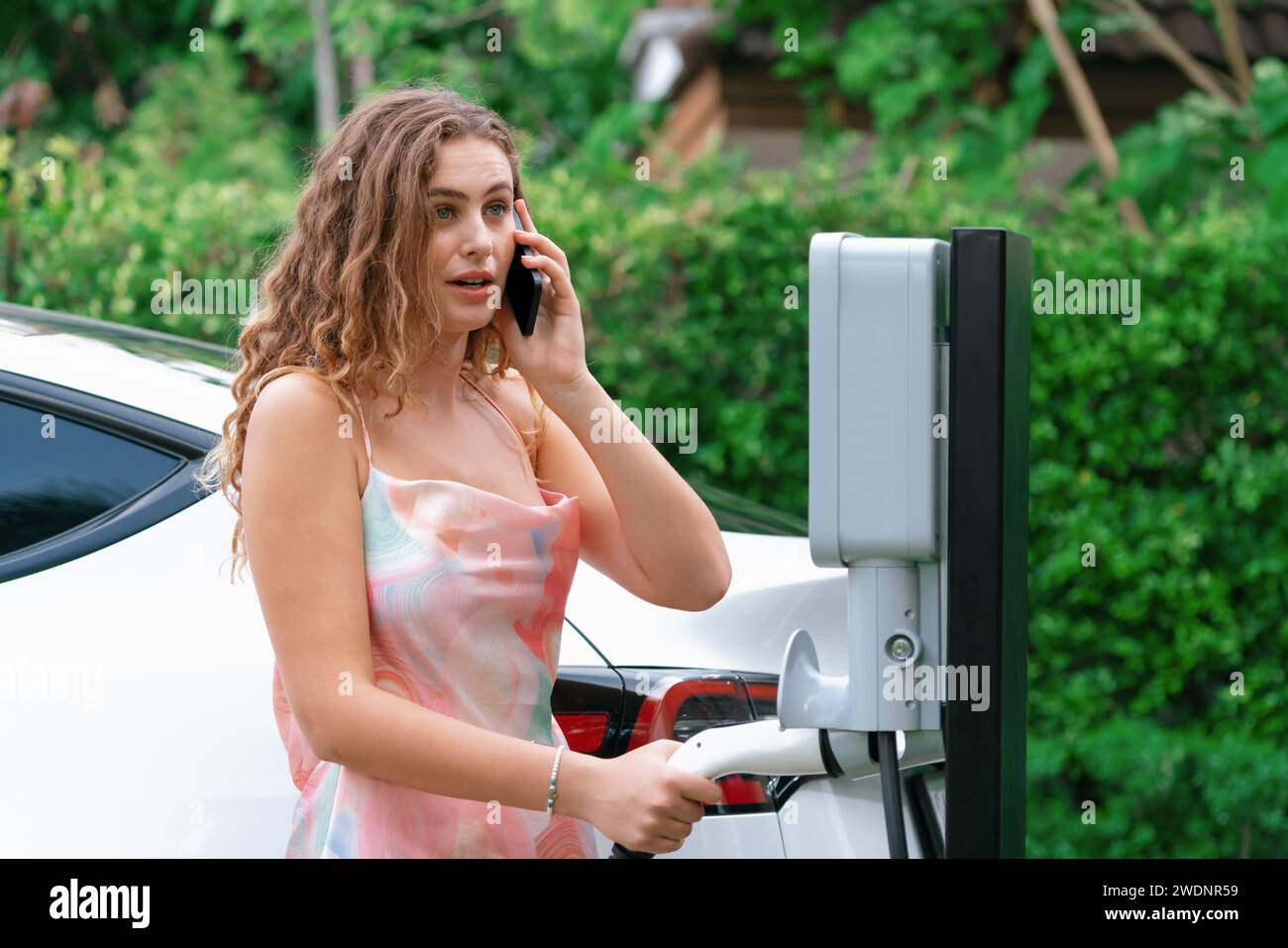 Modern eco-friendly woman recharging electric vehicle from home EV charging station. Innovative ...