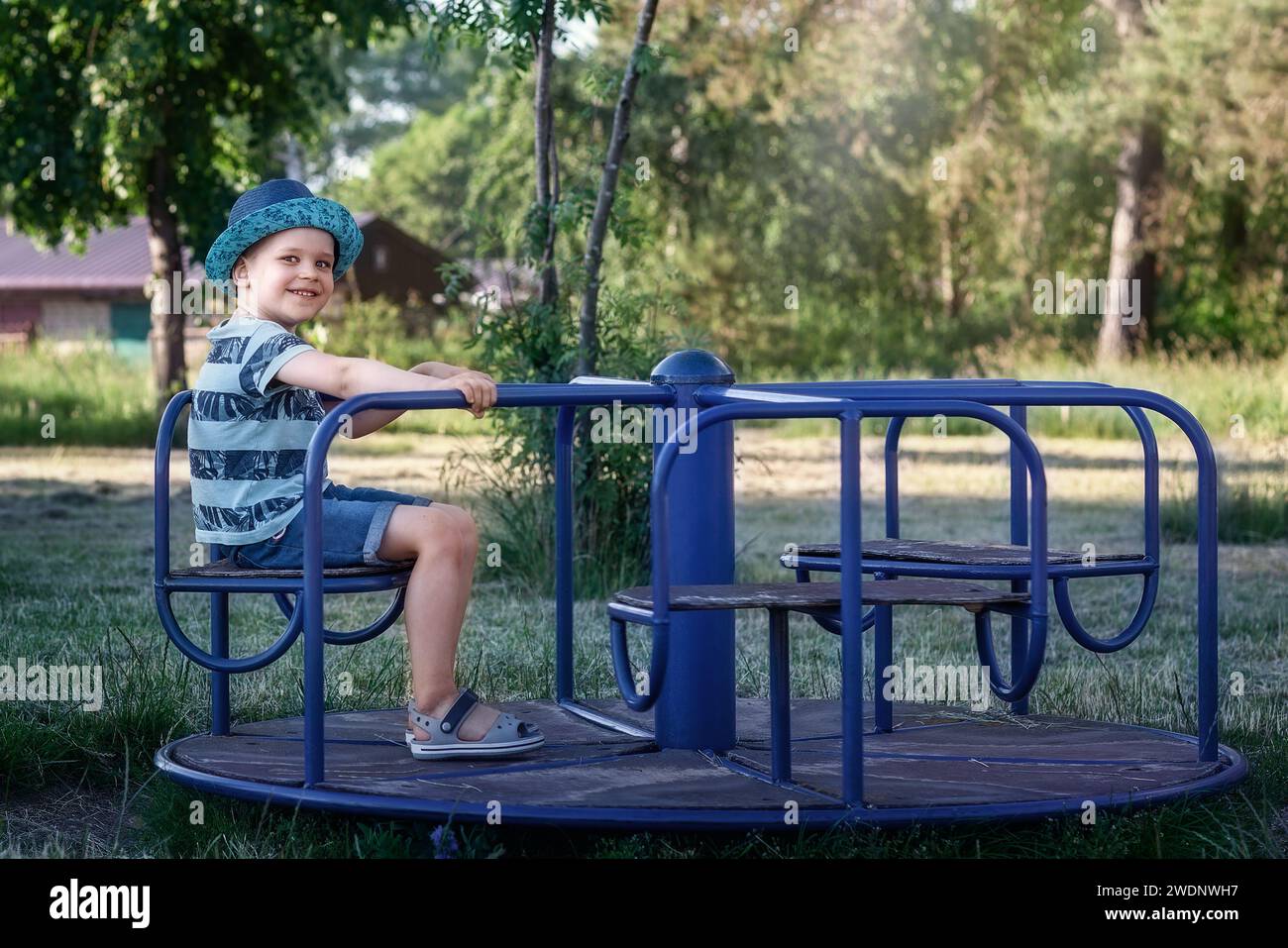 A cheerful and smiling boy spins on a blue merry-go-round in an outdoor ...