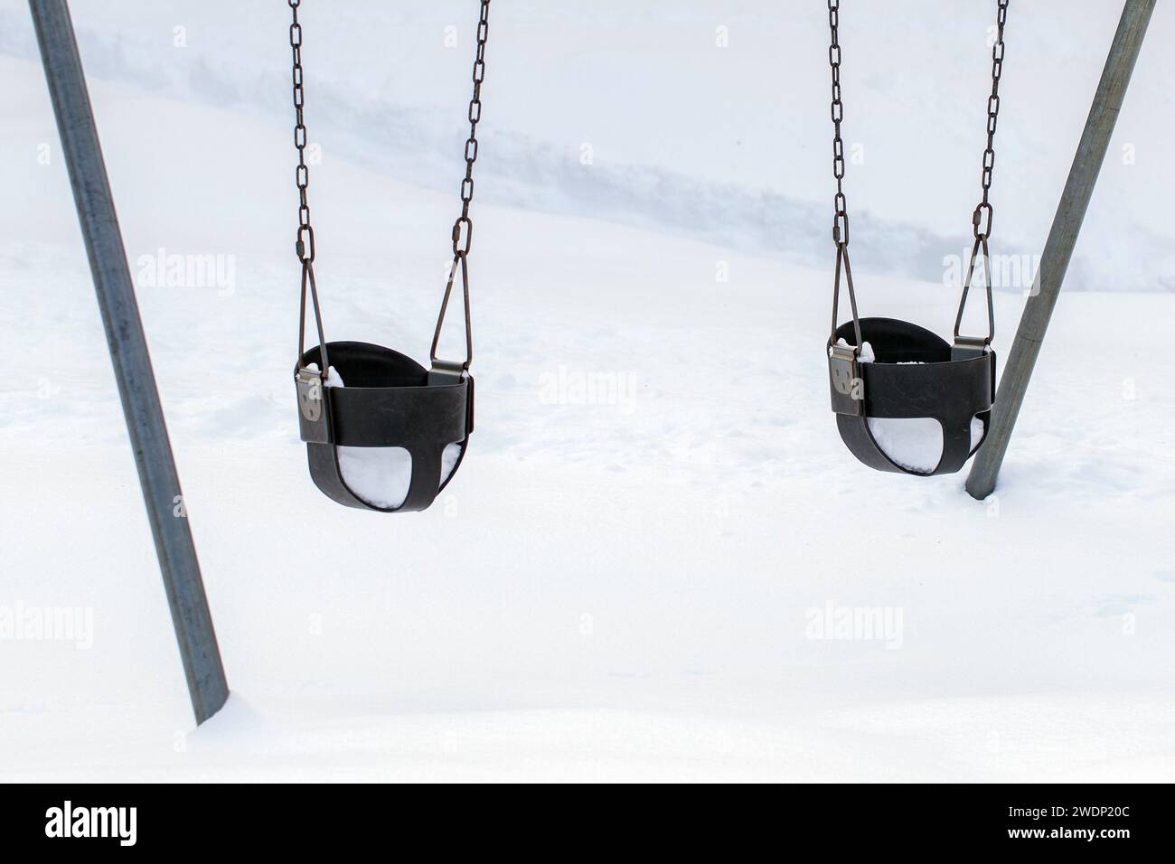 Swings for little children at playground in park, covered with snow in ...