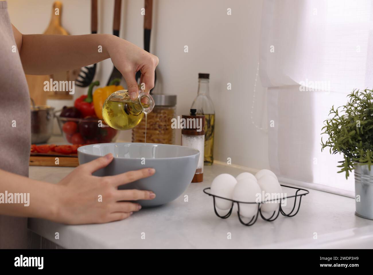 Cooking process. Woman pouring oil from bottle into bowl at light ...