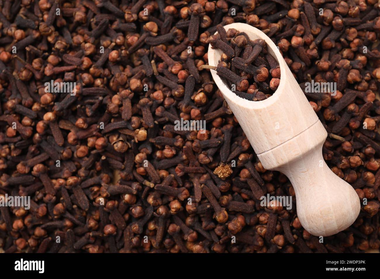Many aromatic cloves and wooden scoop as background, top view. Space ...