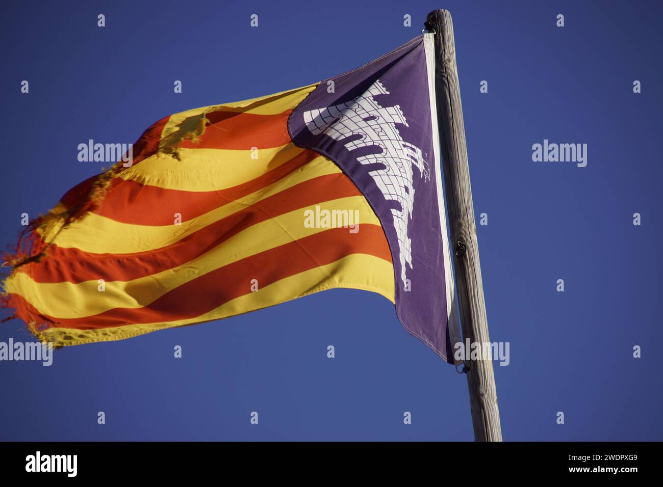 A close-up of the flag of Mallorca on a tall pole against a blue sky ...