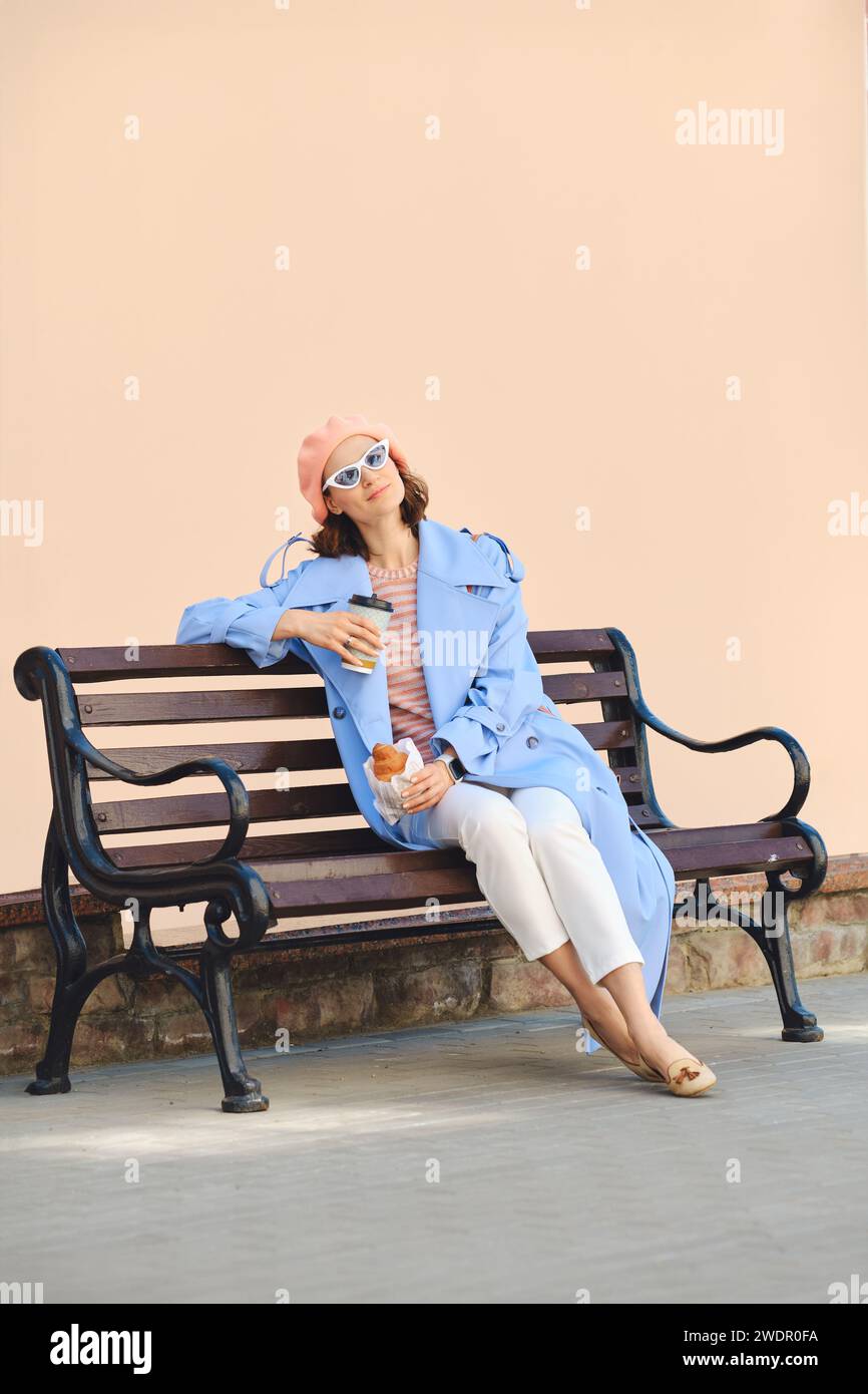 Careless woman in coral beret and blouse, blue raincoat and sunglasses ...